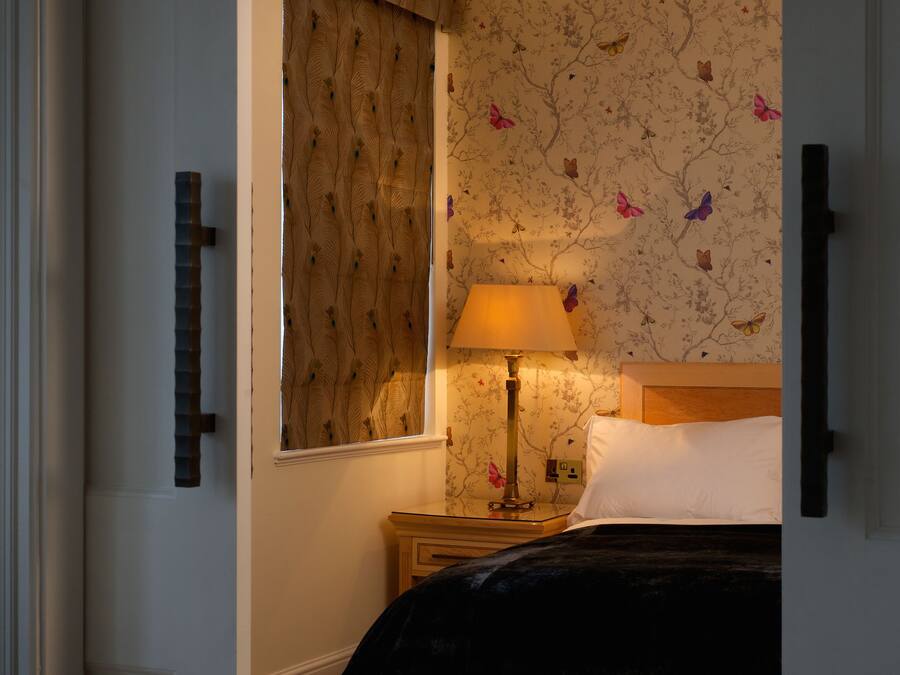 Quarto de hotel com cama, mesa de cabeceira, abajur e janela com cortinas.