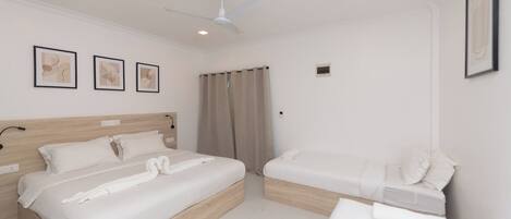 Quarto de hotel com duas camas, um ventilador de teto e três quadros na parede.