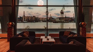 Sala de estar moderna com uma grande janela que dá para uma paisagem urbana e para a água.