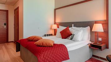 Quarto de hotel com cama, duas luminárias de cabeceira, mesa de cabeceira e manta vermelha.