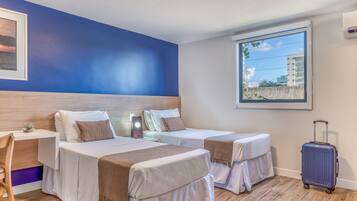 Quarto de hotel com duas camas, uma escrivaninha e uma janela com vista para edifícios.