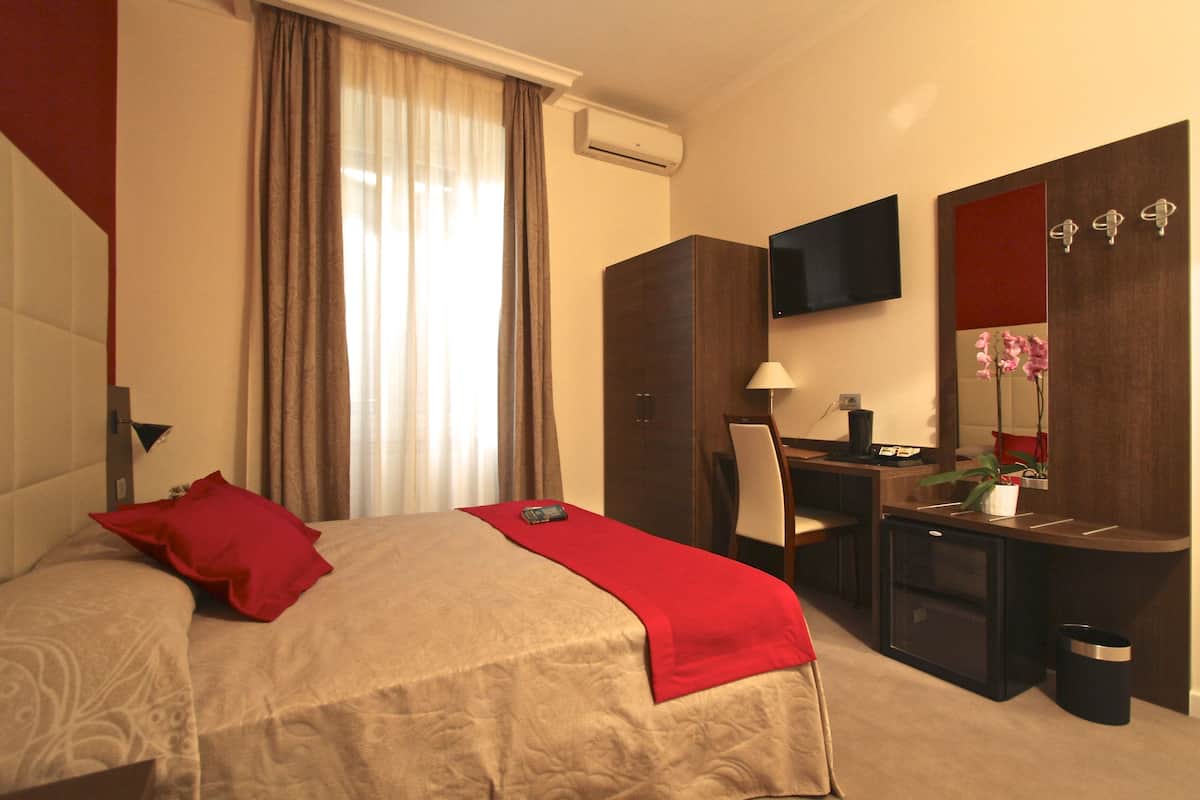 Quarto de hotel com cama, escrivaninha, cadeira, televisão e uma pequena cozinha.