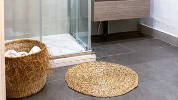 Um banheiro moderno com box de vidro, espelho redondo, toucador de madeira e tapete de fibra natural no chão.