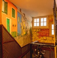 Uma escadaria com corrimão de madeira e uma parede com um mural de edifícios coloridos.