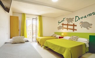 Quarto com duas camas, janela com cortinas amarelas e uma decoração de ovelha com a inscrição 'Sweet Dreams'.