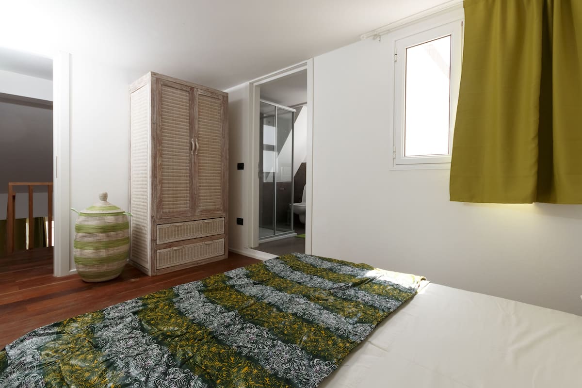 Quarto com cama, guarda-roupa, um vaso grande e janela com cortinas.