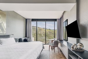 Quarto de hotel moderno com cama grande, escrivaninha e televisão.