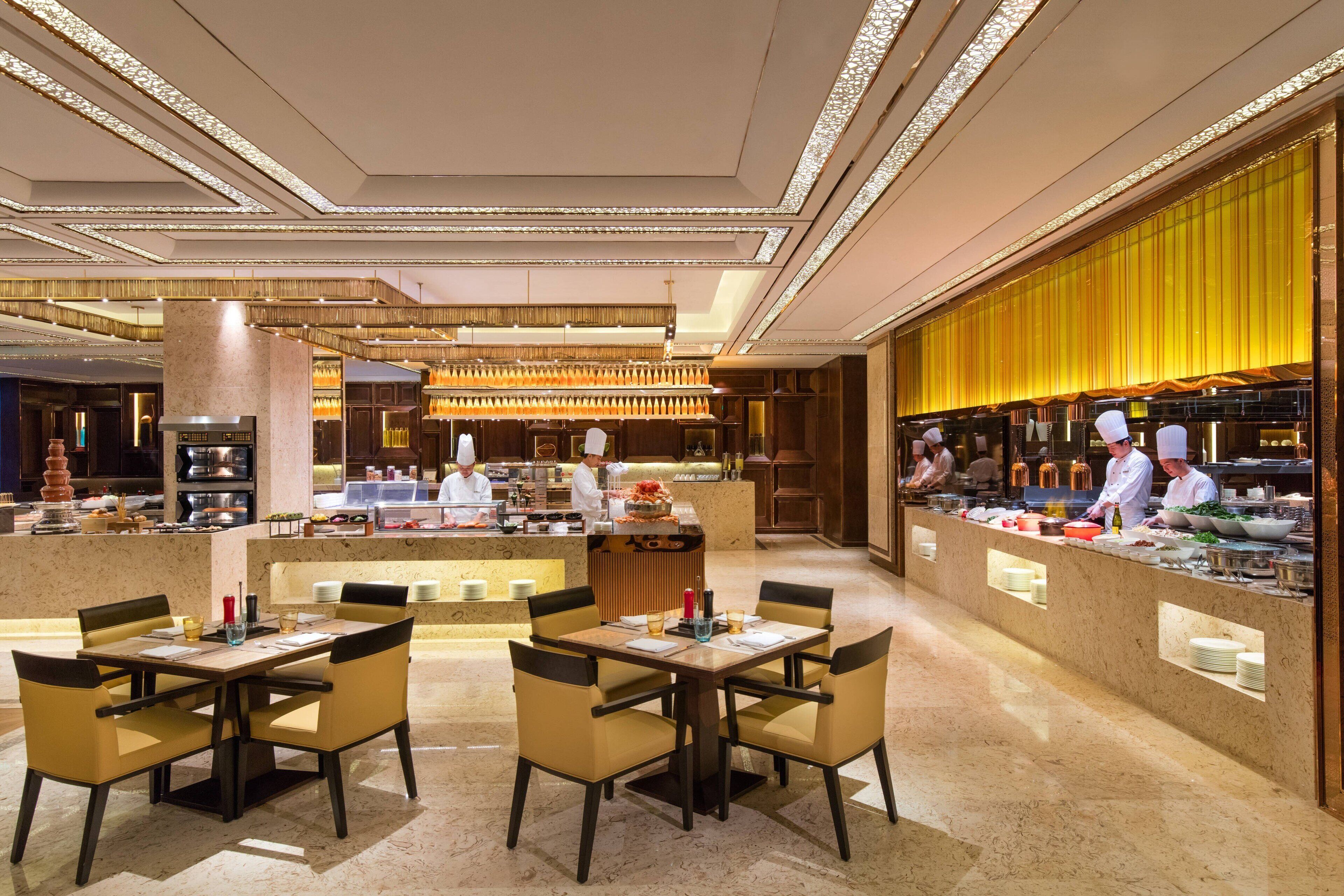 Restaurante moderno com um balcão central, diversas opções de assentos e cozinha à vista, com chefs trabalhando.