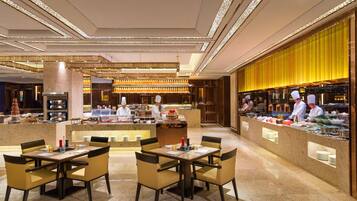 Restaurante moderno com um balcão central, diversas opções de assentos e cozinha à vista, com chefs trabalhando.