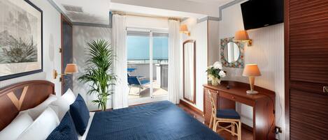 Quarto de hotel com cama, escrivaninha, cadeira, televisão e varanda com vista.