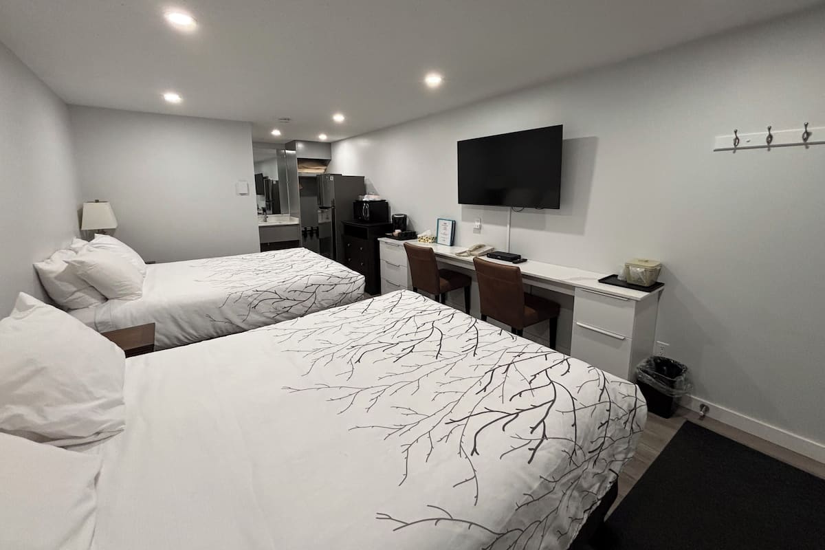 Quarto de hotel com duas camas, uma escrivaninha, uma televisão e um espelho.