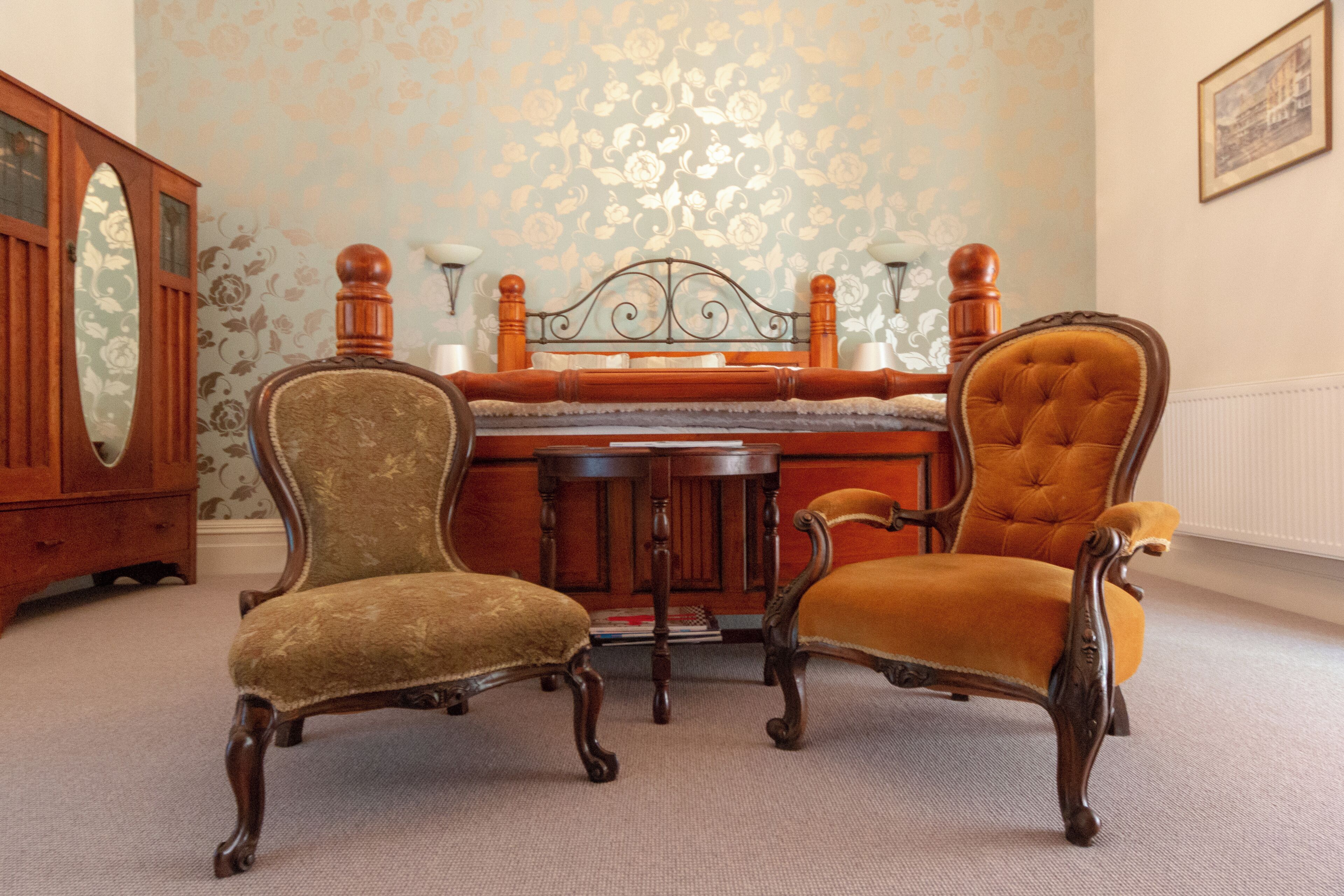 Quarto com duas poltronas estofadas, uma mesa de madeira e papel de parede estampado.