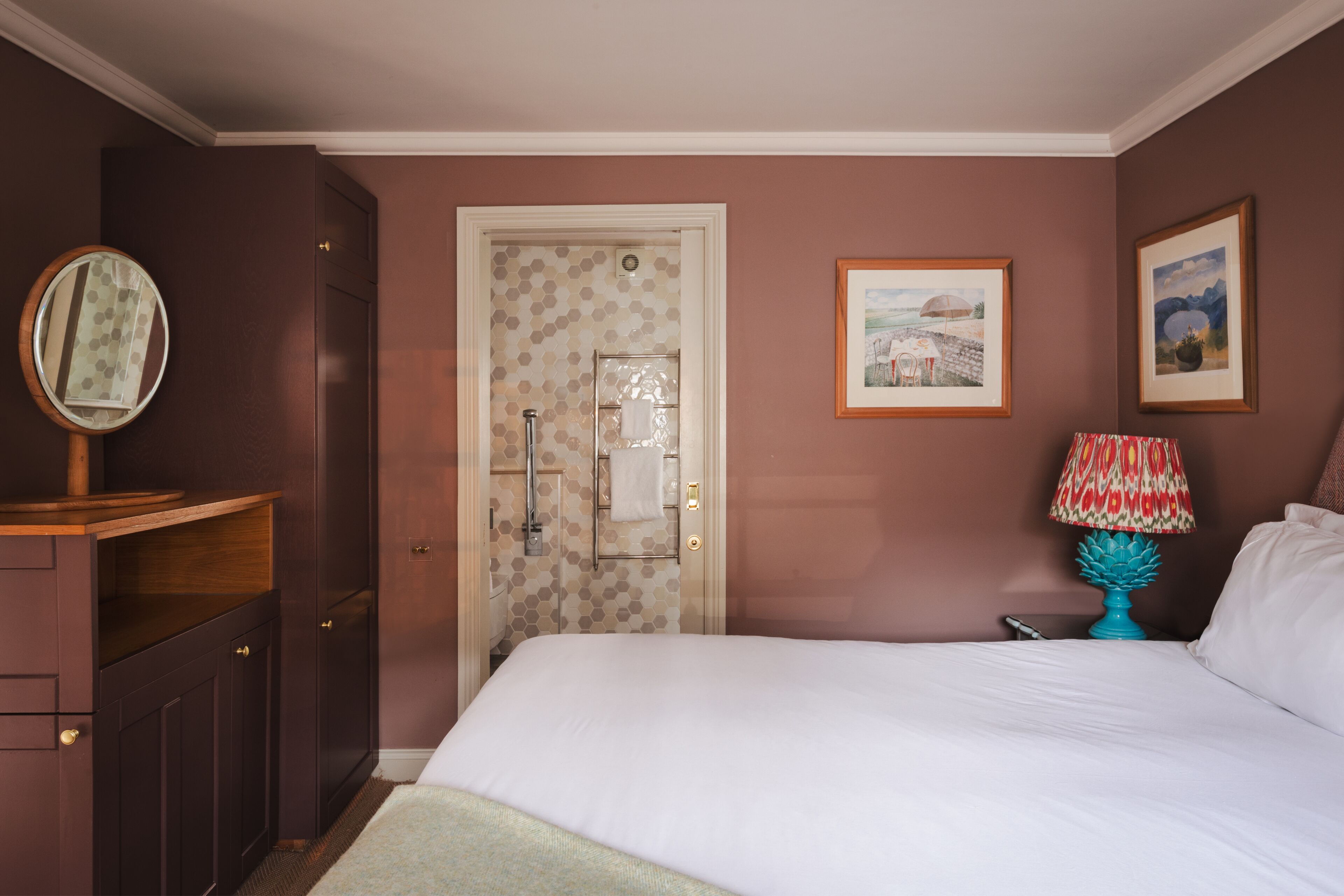 Quarto de hotel com cama, banheiro com chuveiro, espelho e luminária na parede.