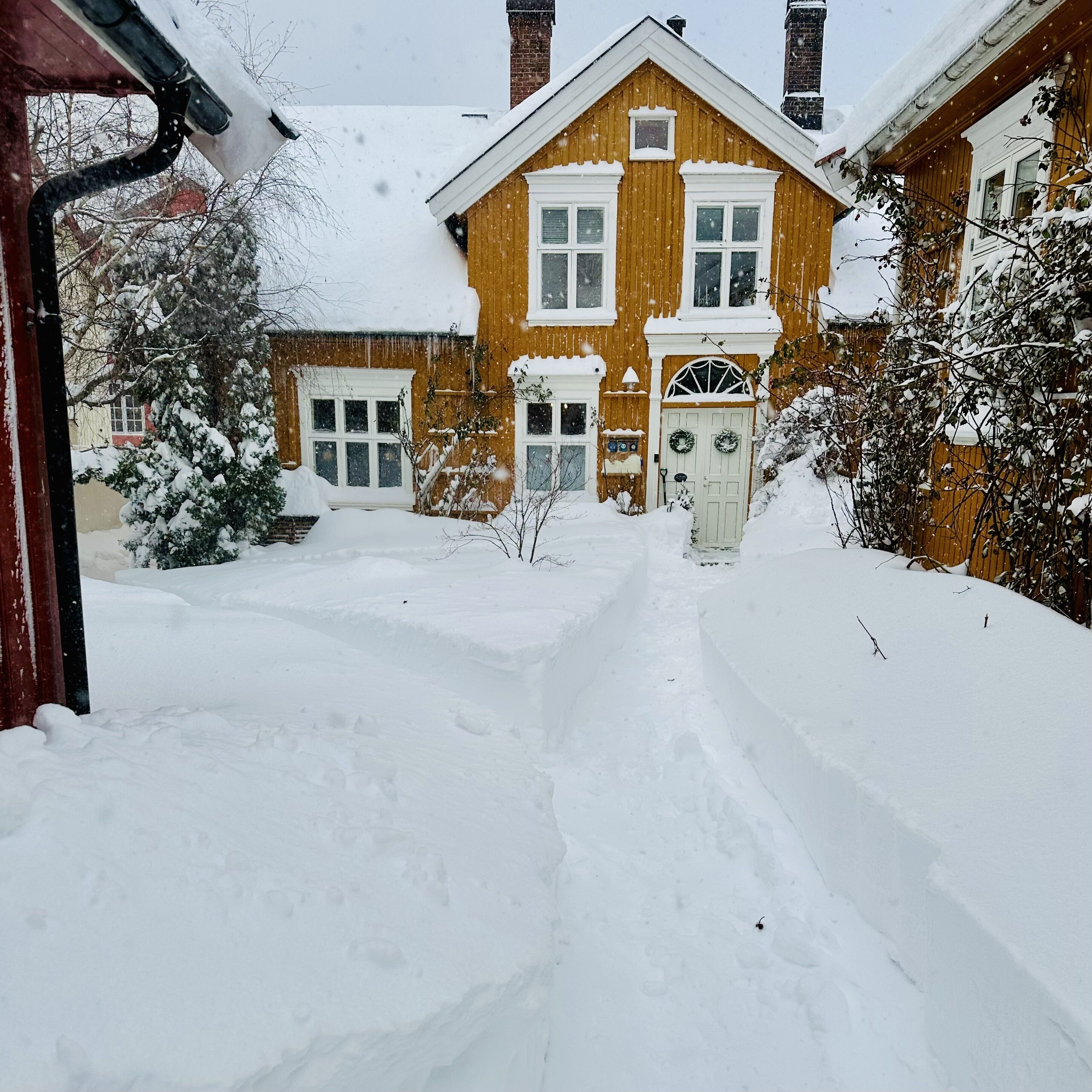 Uma casa de madeira coberta de neve, com porta e janelas, rodeada por neve.