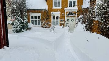 Uma casa de madeira coberta de neve, com porta e janelas, rodeada por neve.