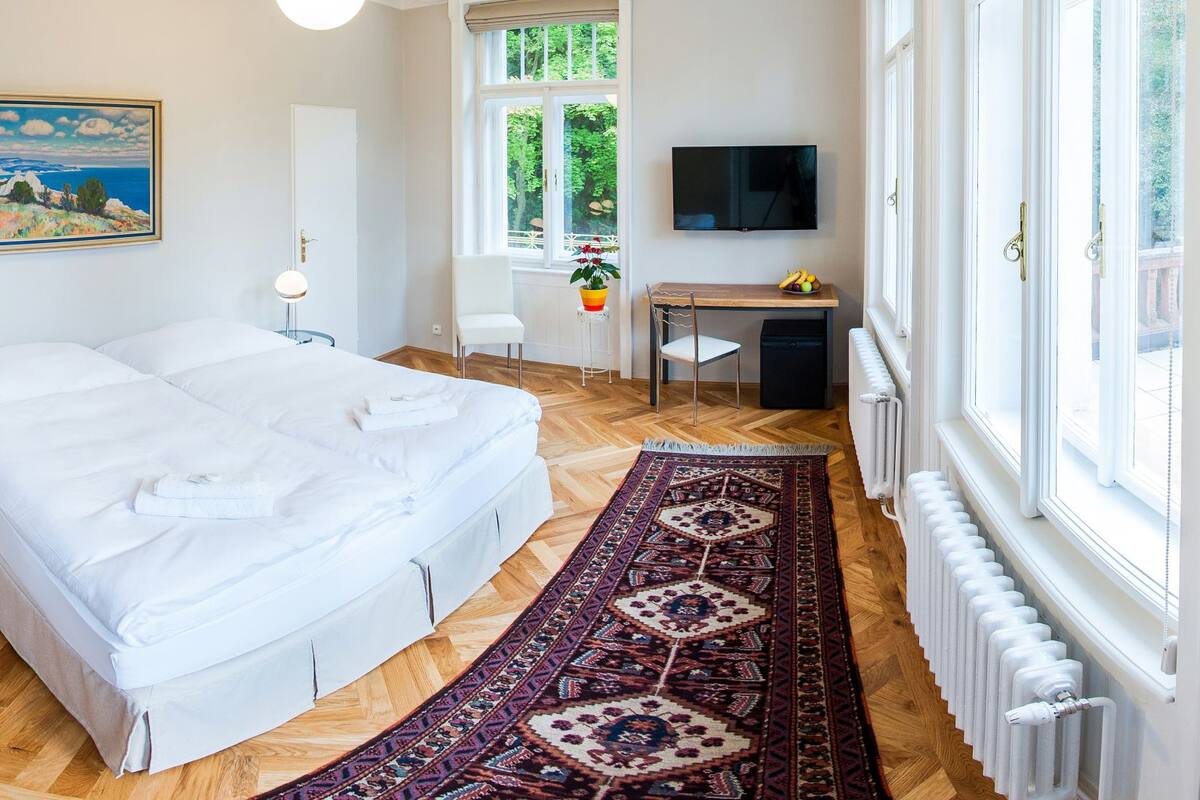 Quarto com uma cama grande, uma escrivaninha, uma televisão e vista para o verde lá fora.