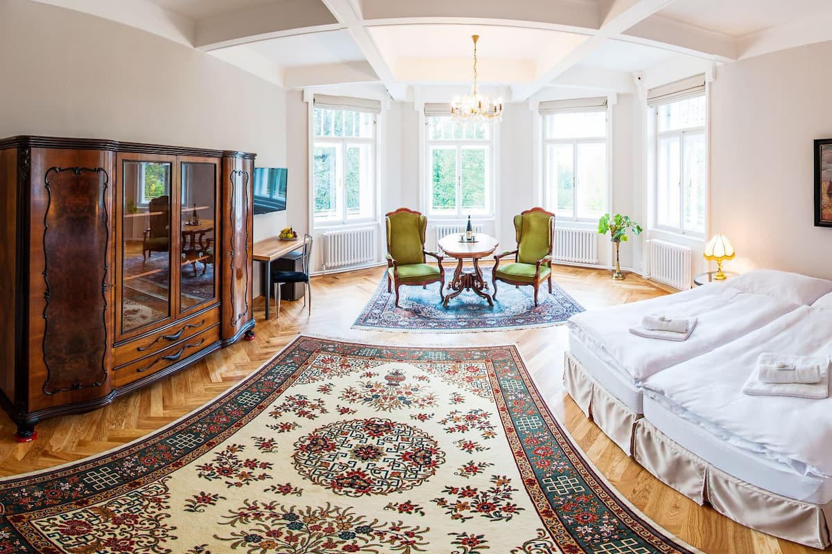 Um quarto espaçoso com uma cama grande, um armário de madeira, uma mesa de jantar com cadeiras e um lustre.