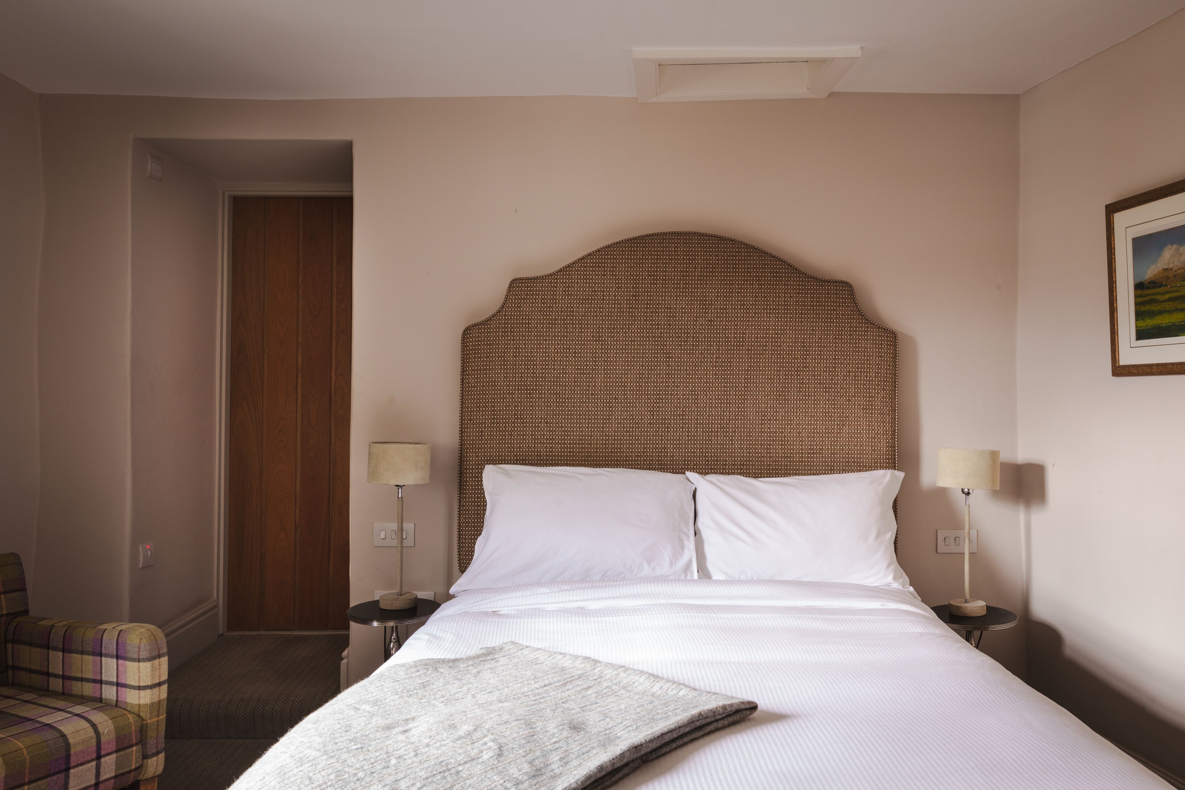 Quarto de hotel com uma cama, duas mesas de cabeceira, uma cadeira e uma porta.
