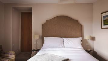 Quarto de hotel com uma cama, duas mesas de cabeceira, uma cadeira e uma porta.