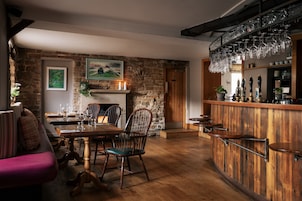 Interior rústico com mesa de jantar de madeira, cadeiras, área de bar com adega e lareira.