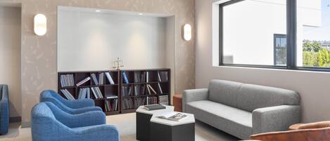 Uma sala de estar moderna com um sofá cinzento, poltronas azuis, uma mesa de centro preta e uma estante de livros.