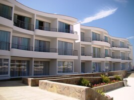 Um hotel com vários andares, varandas, janelas amplas e um jardim com plantas e flores.