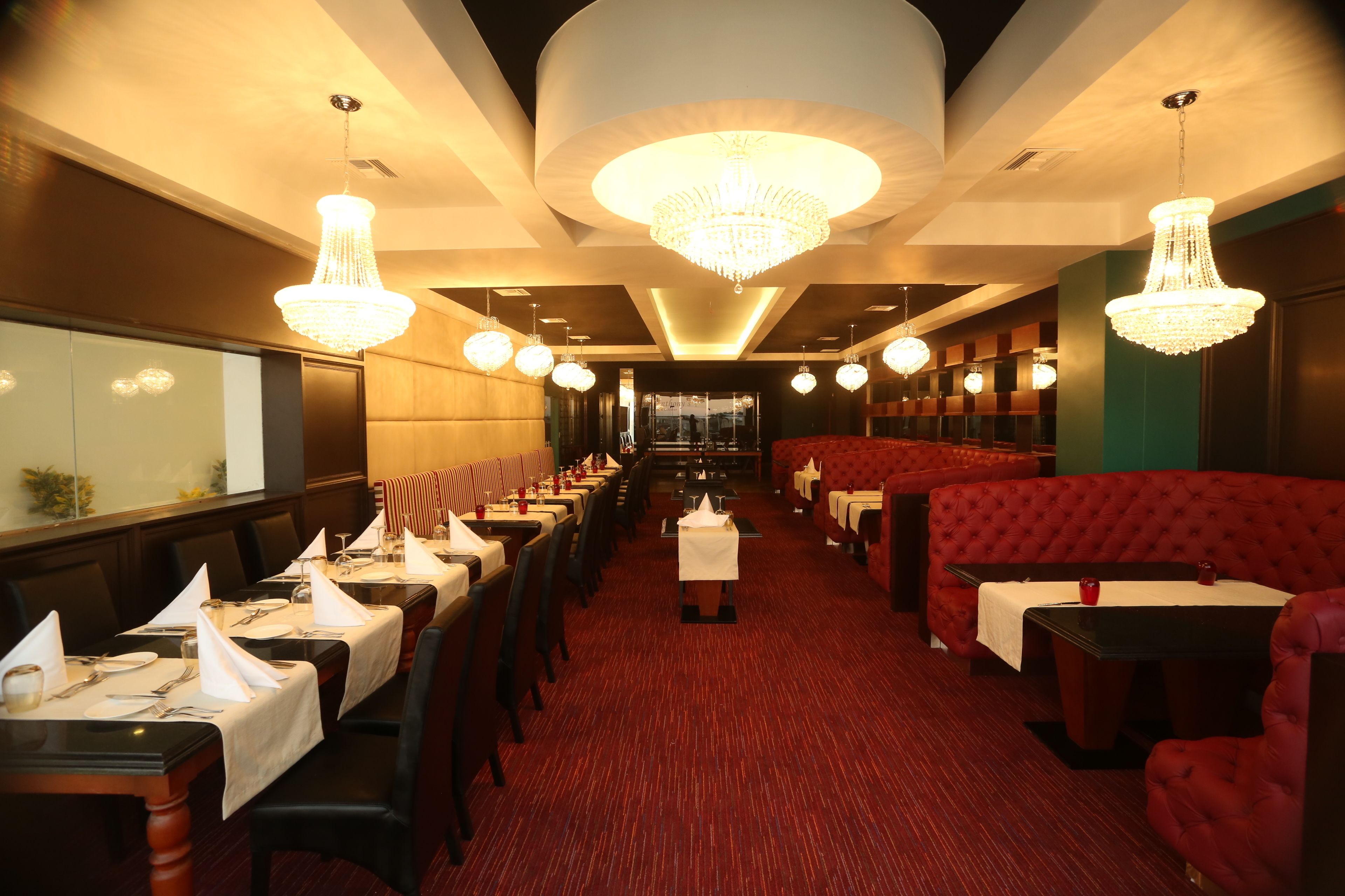 Restaurante com várias mesas, assentos estofados em vermelho e lustres.