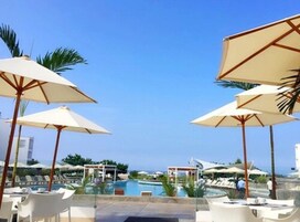 Uma área à beira da piscina com guarda-sóis, espreguiçadeiras e vista para o oceano.