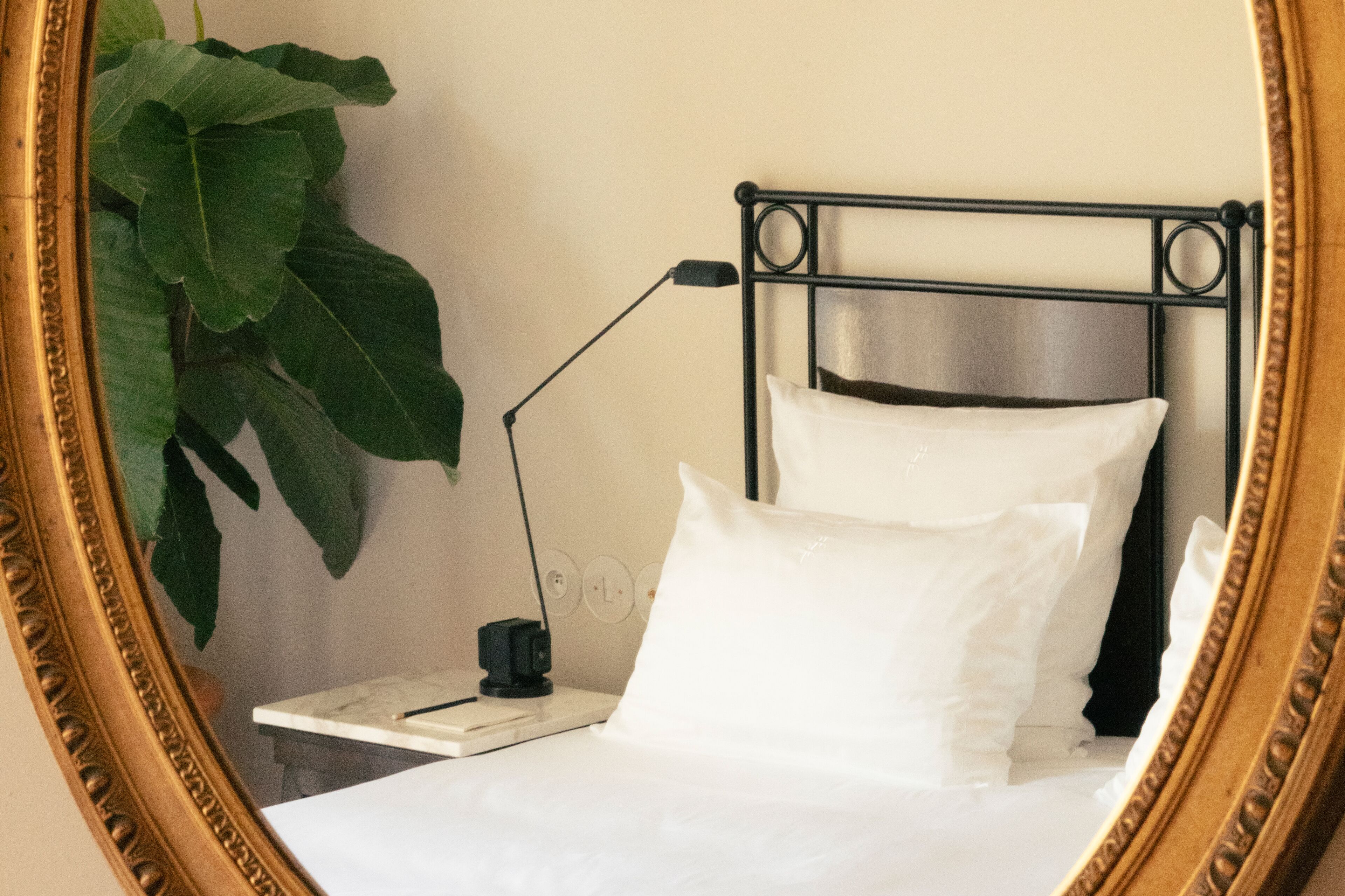 Uma cama com roupa de cama branca, cabeceira de metal preto e mesa de cabeceira com abajur e tomada.