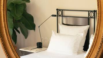 Uma cama com roupa de cama branca, cabeceira de metal preto e mesa de cabeceira com abajur e tomada.