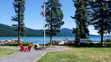 Vista do lago com cadeiras Adirondack vermelhas, um mastro com a bandeira americana e uma placa indicando 'Shelter Cove Resort'.