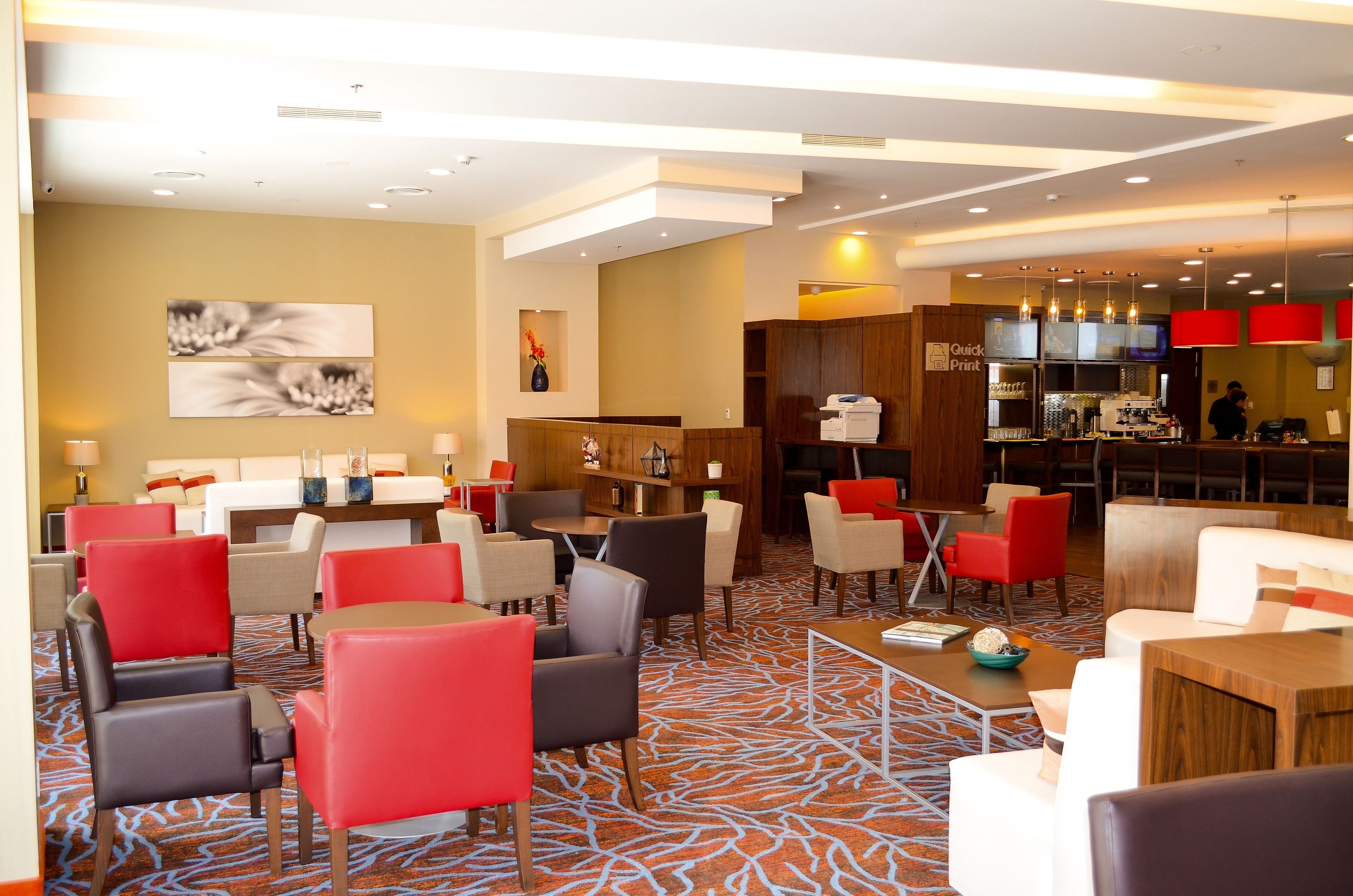 Um saguão de hotel com várias áreas de estar, uma mesa de recepção e um bar.