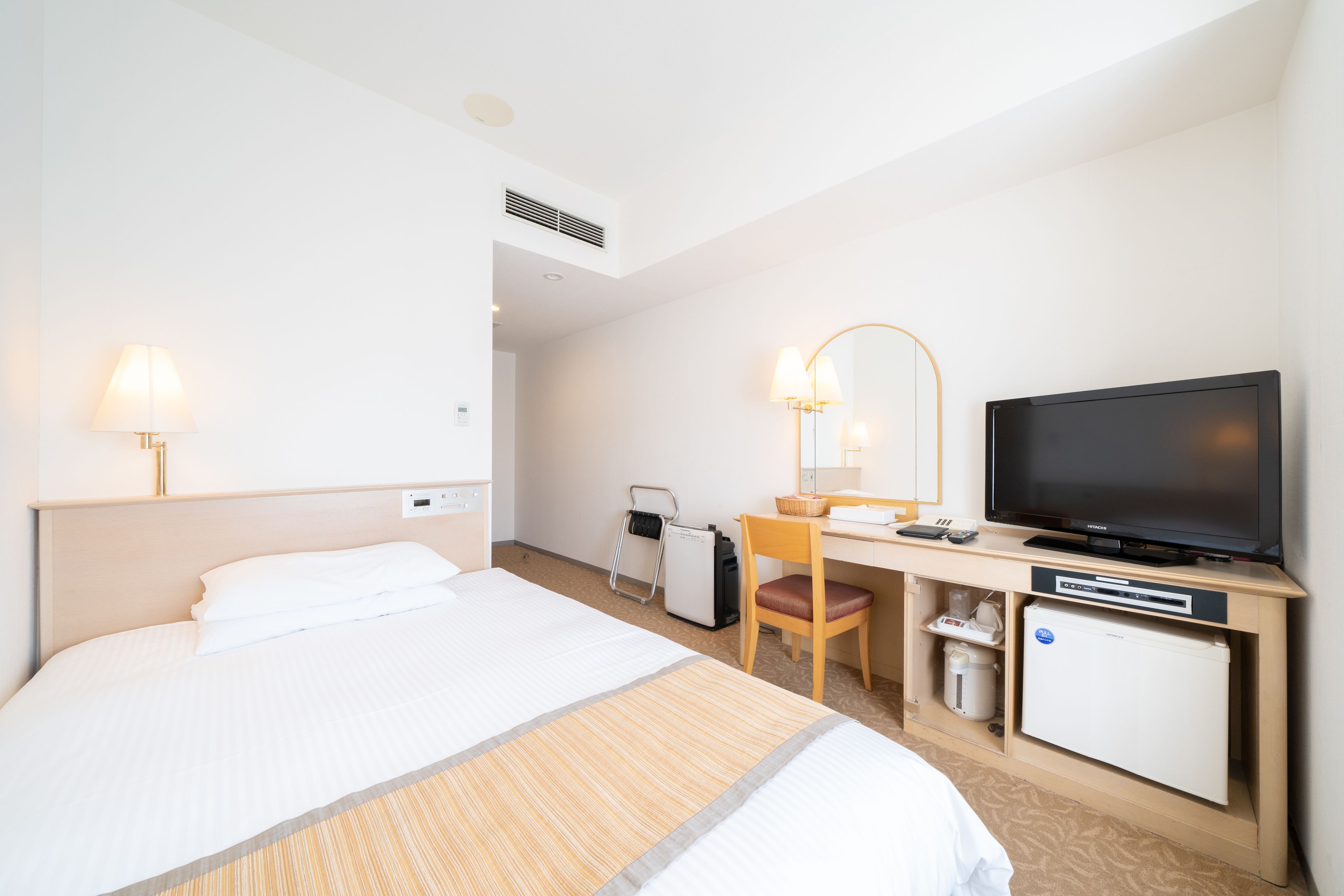 Quarto de hotel com cama, escrivaninha, televisão e pequeno frigorífico.