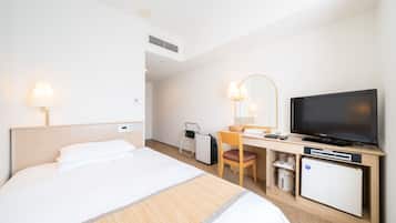 Quarto de hotel com cama, escrivaninha, televisão e pequeno frigorífico.