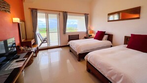 Quarto de hotel com duas camas, uma escrivaninha com televisão e varanda com cortinas.