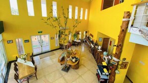 Um hall espaçoso com teto alto, várias janelas e uma área de estar central com uma árvore.