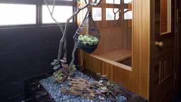 Quarto com porta de madeira, gaiola de pássaro suspensa com folhagem, prateleira de madeira e chão revestido de pedrinhas.
