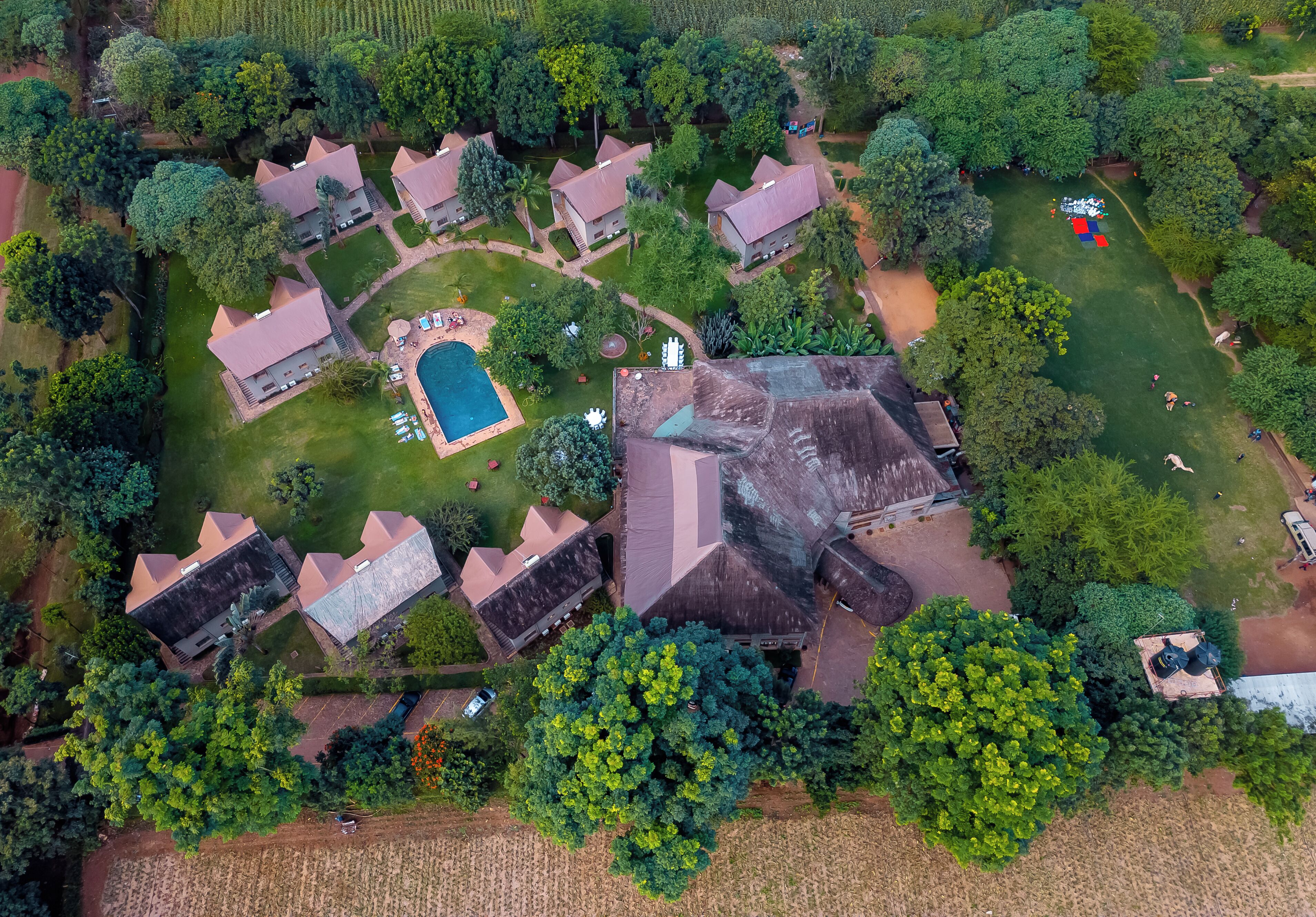 Vista aérea de um resort com vários edifícios, piscina e vegetação exuberante ao redor.
