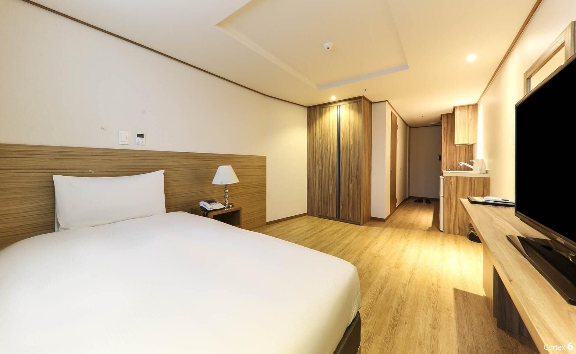 Quarto de hotel com uma cama grande, mesa de cabeceira com abajur, televisão e guarda-roupa de madeira.