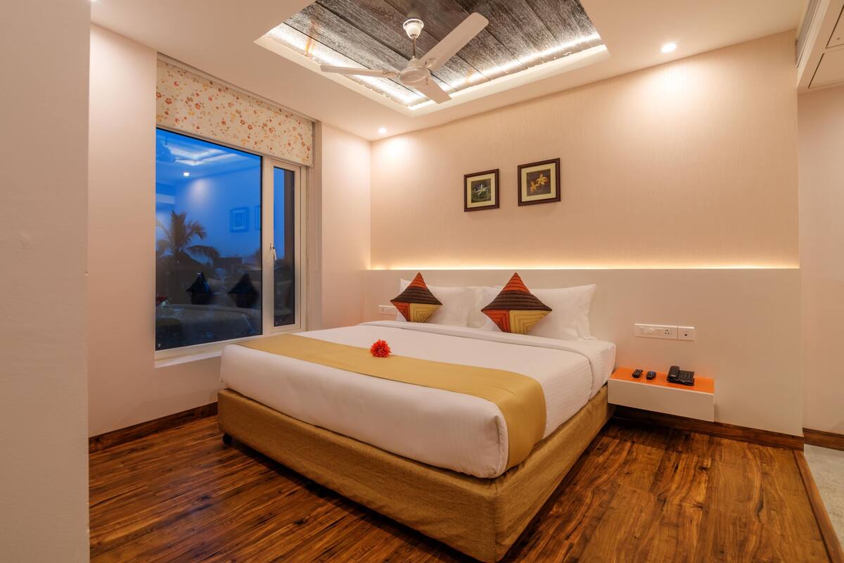 Quarto de hotel moderno com uma cama grande, piso de madeira, um claraboia e vista noturna pela janela.