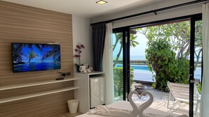Quarto de hotel moderno com uma cama grande, uma TV na parede, vista para o oceano e uma varanda com um travesseiro em formato de cisne branco.