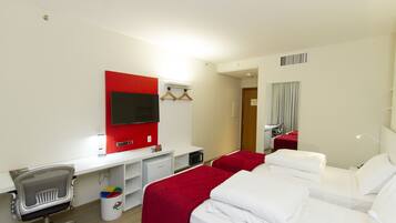 Quarto de hotel com duas camas, uma escrivaninha, uma cadeira, uma televisão e um guarda-roupa.