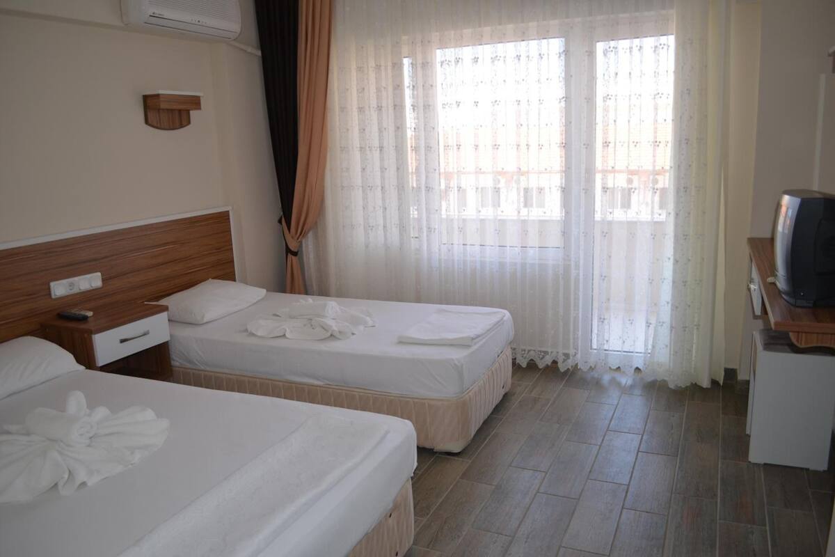Quarto de hotel com duas camas, televisão e uma pequena cozinha equipada.