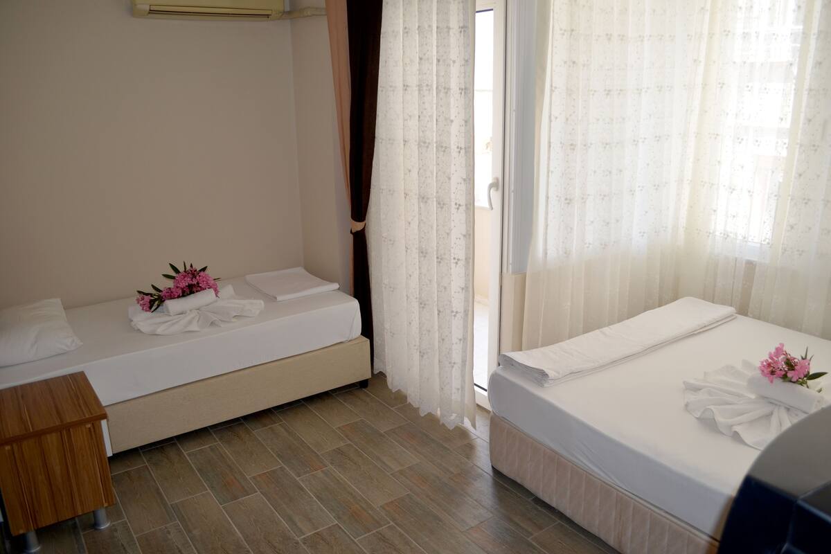Quarto de hotel com duas camas, cada uma com uma colcha branca bem esticada e flores cor-de-rosa.