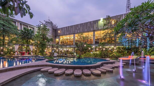 Uma área de piscina com várias fontes, espaços para relaxar e vegetação exuberante.