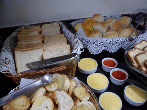 Buffet com diversos tipos de pão e pães de enrolar, além de pequenas embalagens de manteiga e geleia.