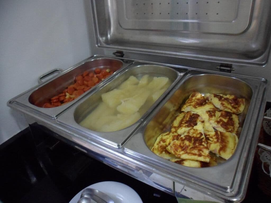 Buffet com diversos alimentos, incluindo cenouras, purê de batatas e ovos fritos.