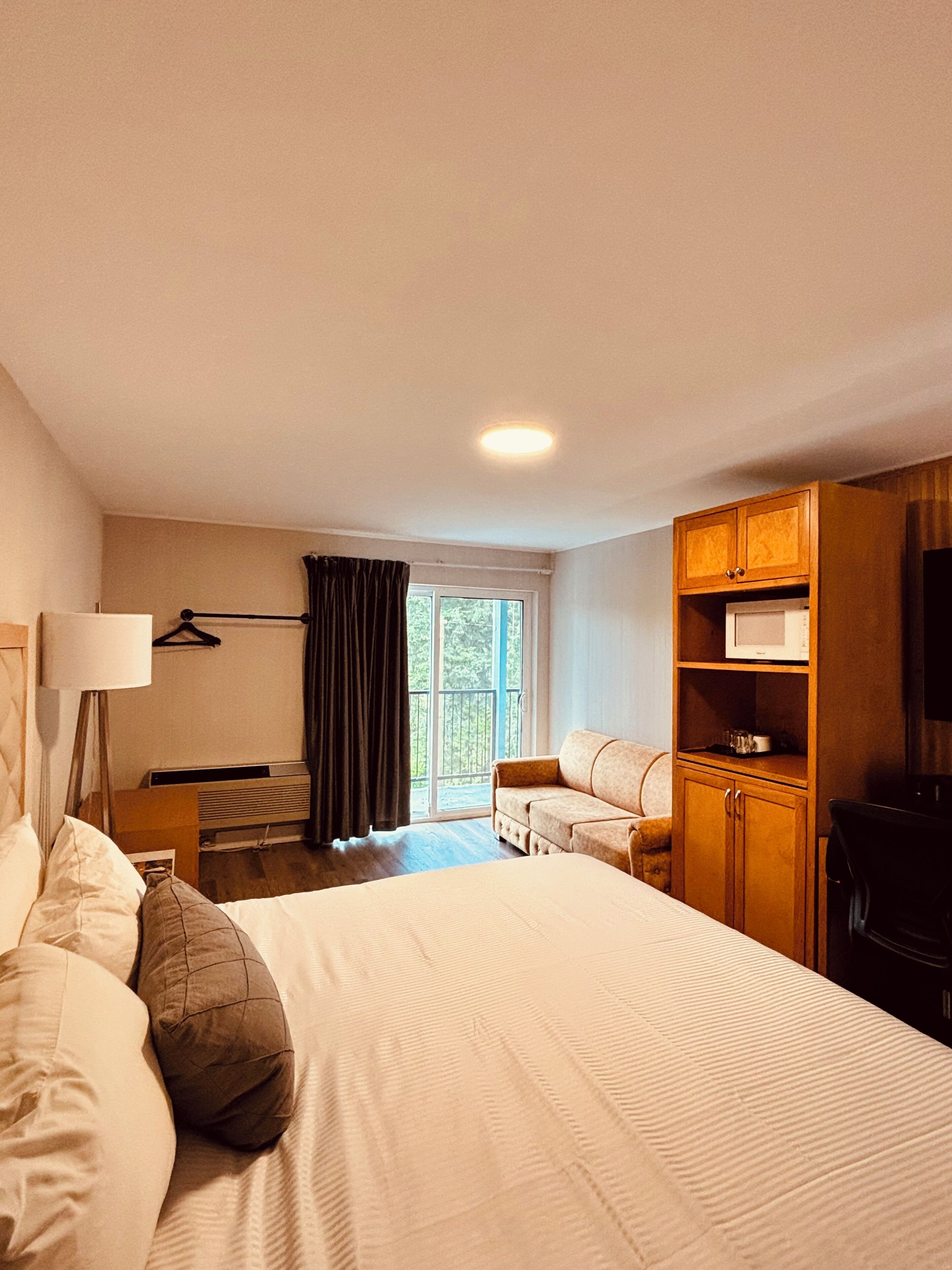 Quarto de hotel com uma cama grande, um sofá, uma escrivaninha, uma televisão e uma janela com cortinas.