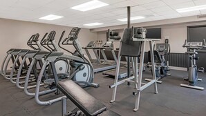 Uma academia com várias esteiras, elípticos e um banco de musculação.