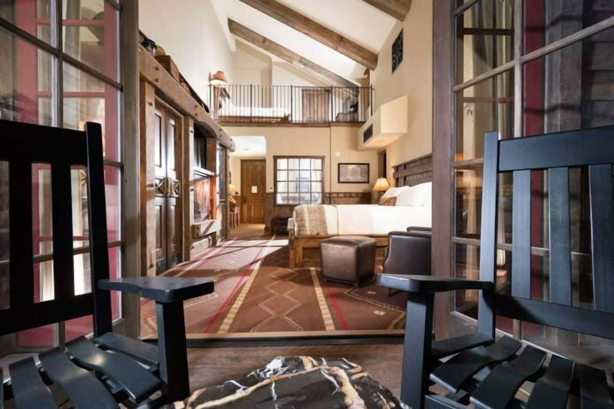 Quarto de hotel com cama, escrivaninha, cadeira, janela e varanda.